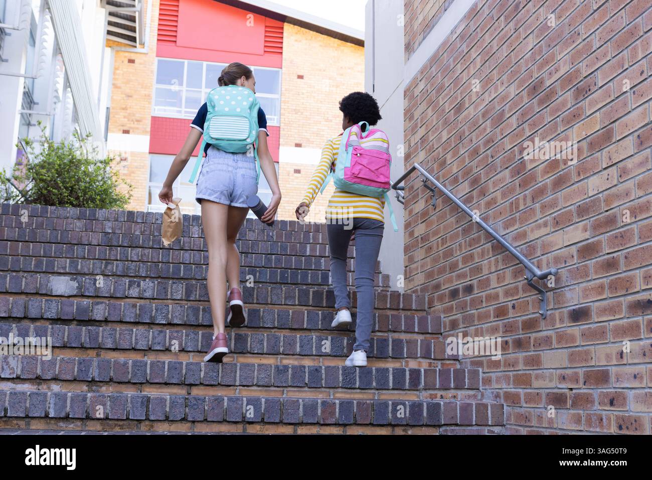Walking up stairs, two diverse girls with backpacks heading to school ...