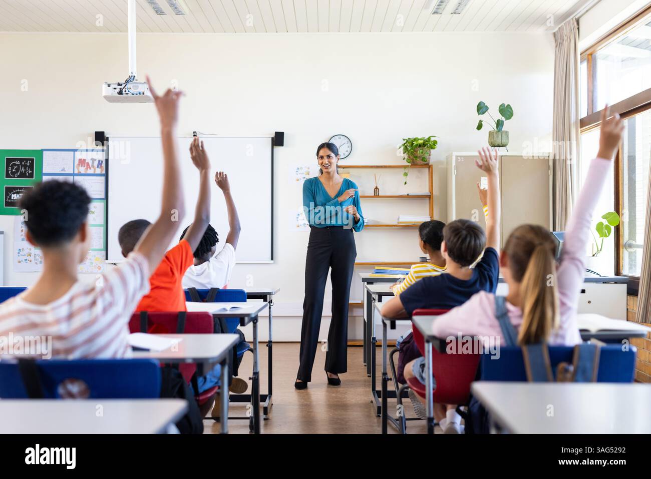Indian female teacher in classroom, students raising hands to answer ...