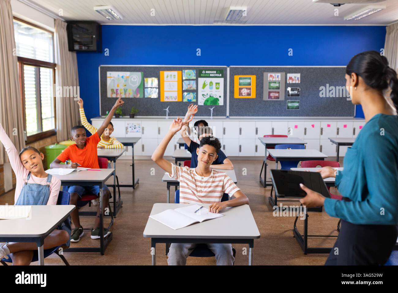 In school, students raising hands in classroom while Indian female ...