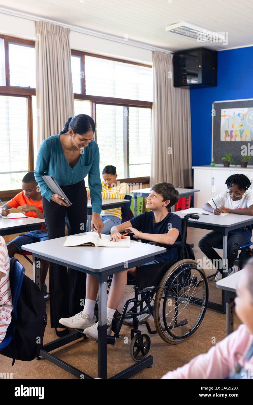 In school, Indian female teacher assisting student in wheelchair with ...