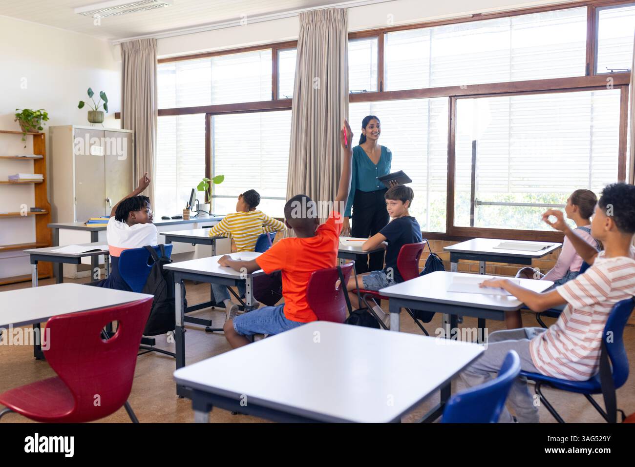 In school, Indian female teacher holding tablet and students raising ...