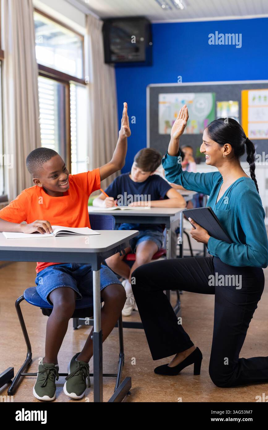 In school, Indian female teacher high-fiving student while holding ...