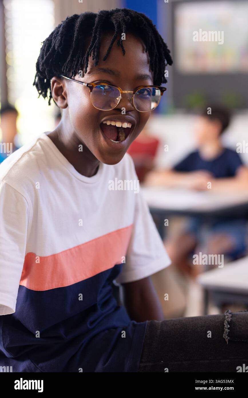 In school, excited student wearing glasses smiling in classroom with ...