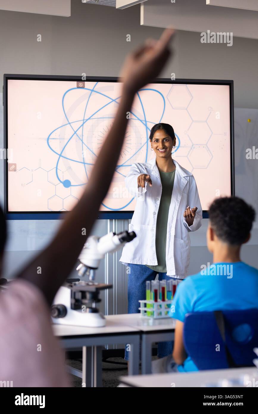 In school, Indian female teacher in lab coat pointing at student in ...