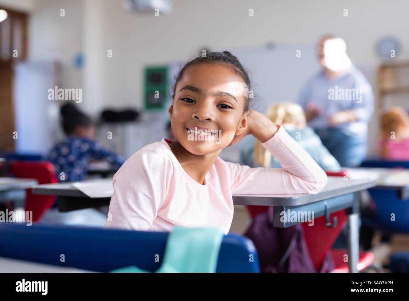Smiling girl sitting at desk in school classroom, looking at camera ...