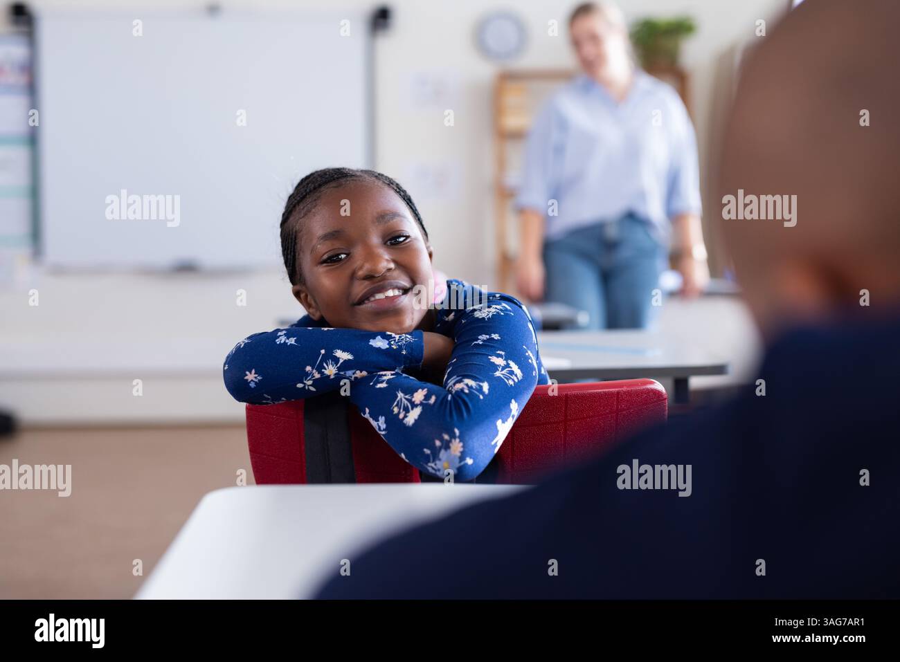 Smiling african american girl in school classroom leaning on chair ...