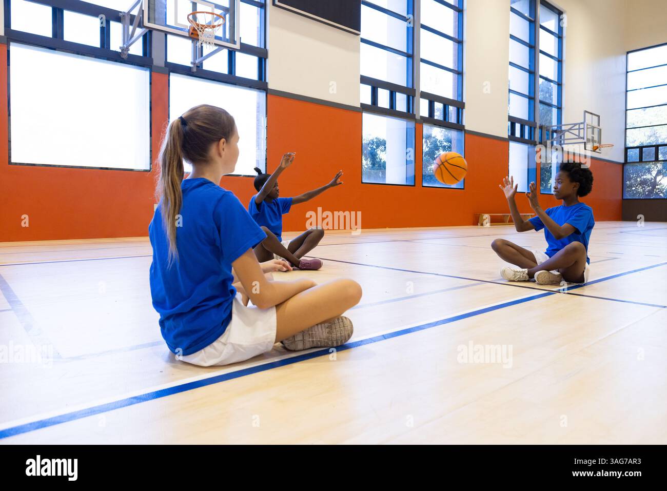 Playing basketball in school gym, diverse girls passing ball and having ...