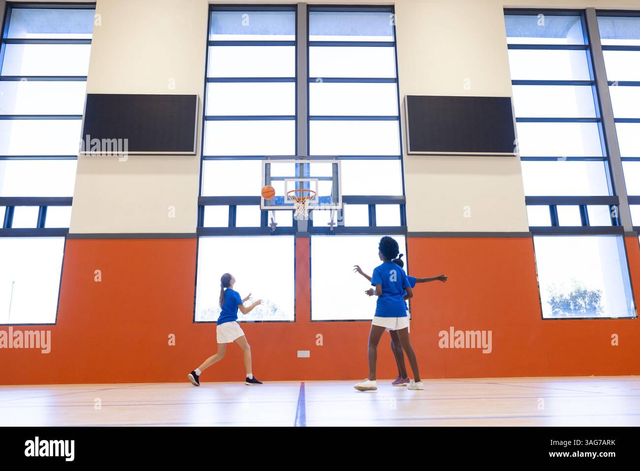 Playing basketball in school gym, diverse girls shooting hoops and ...