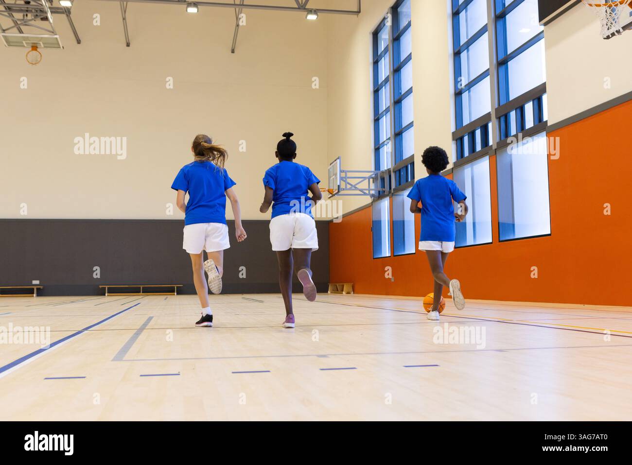 Running in gym, three diverse girls in blue shirts and white shorts at ...