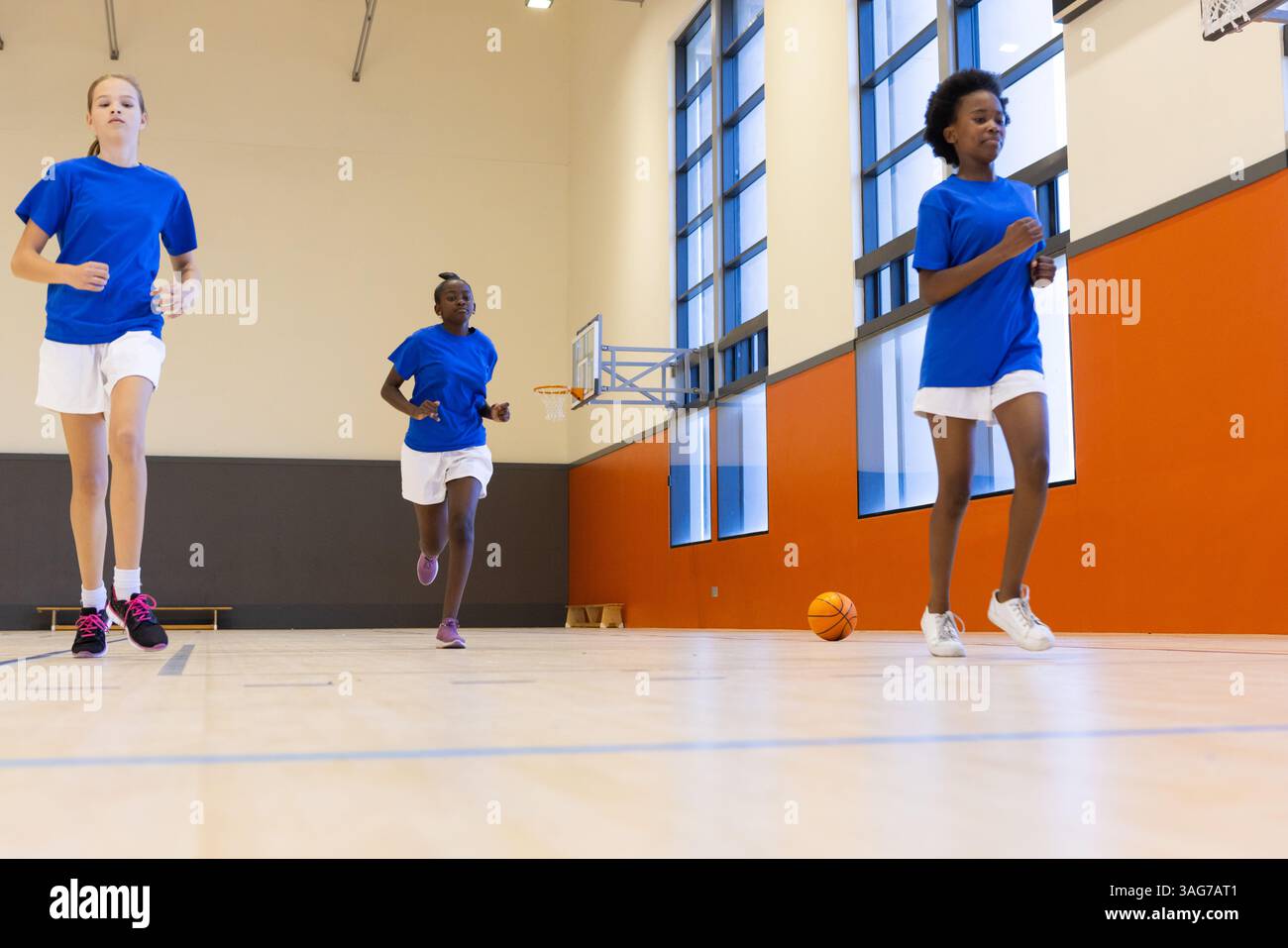 Running in gym, three diverse girls in blue shirts exercising at school ...