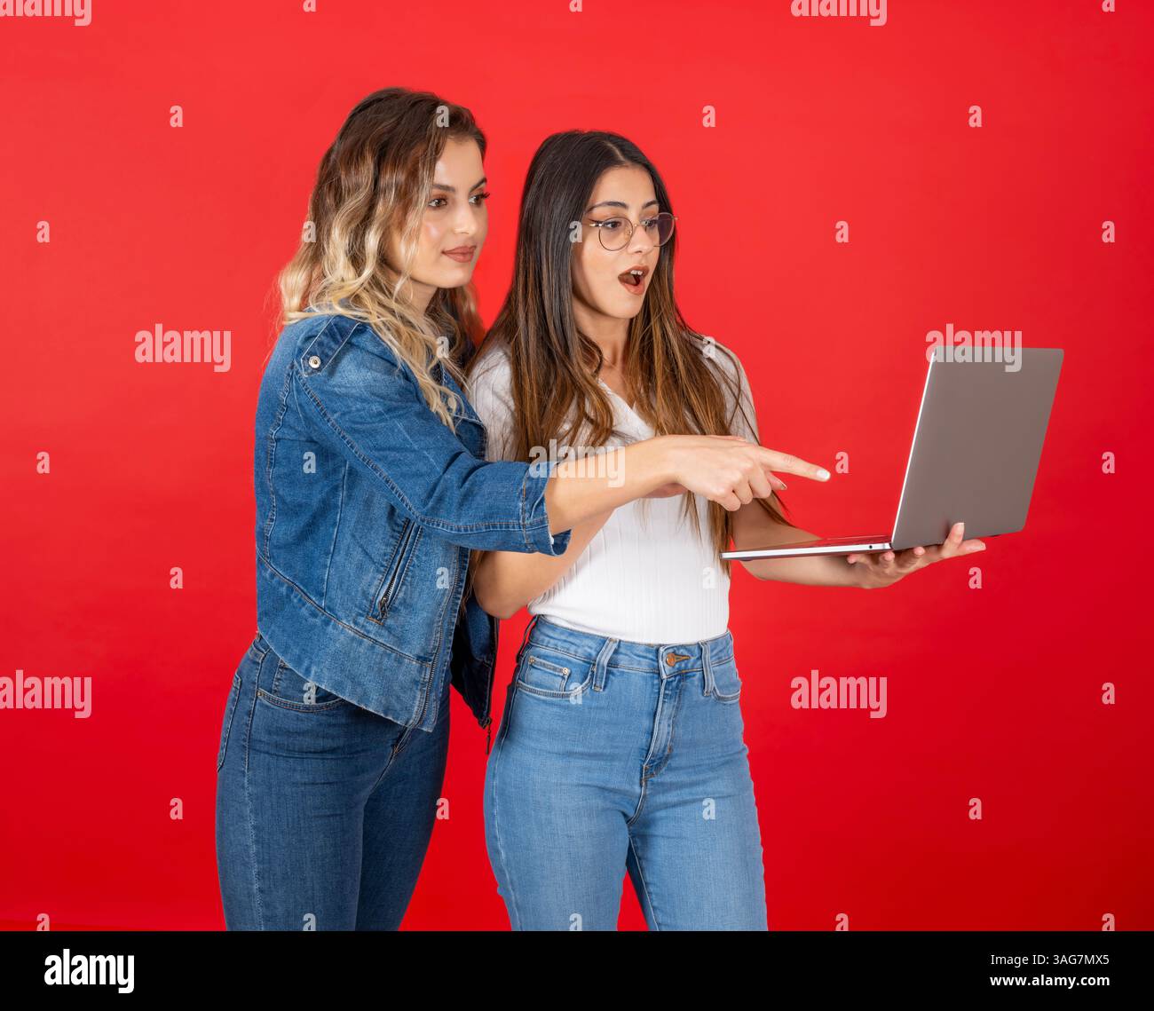Two women using laptop together, pointing at computer screen over red ...