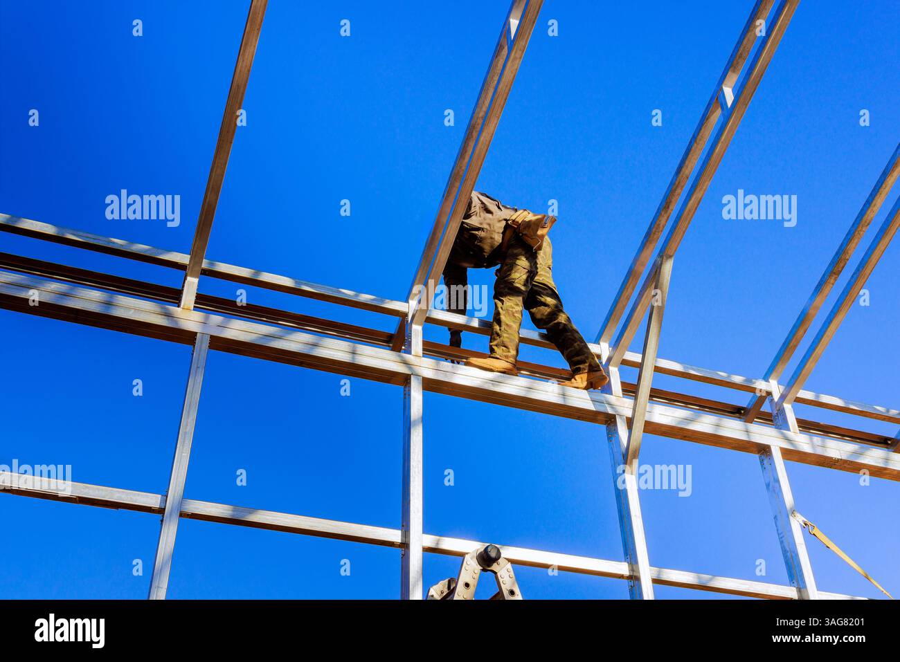 Construction worker is positioned high on steel framework, carefully ...