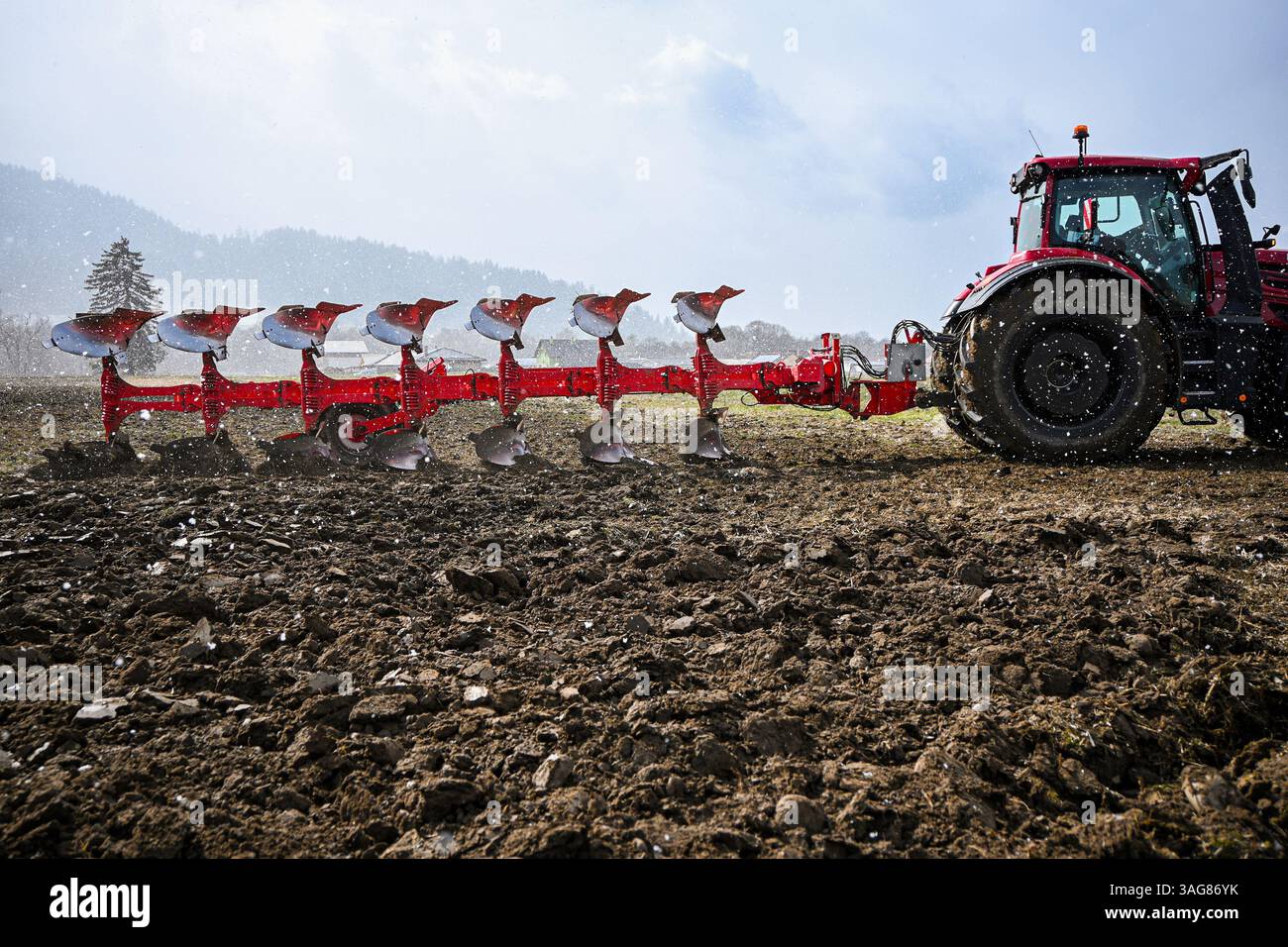 Red tractor pulling plow in field during snowfall, preparing soil for ...