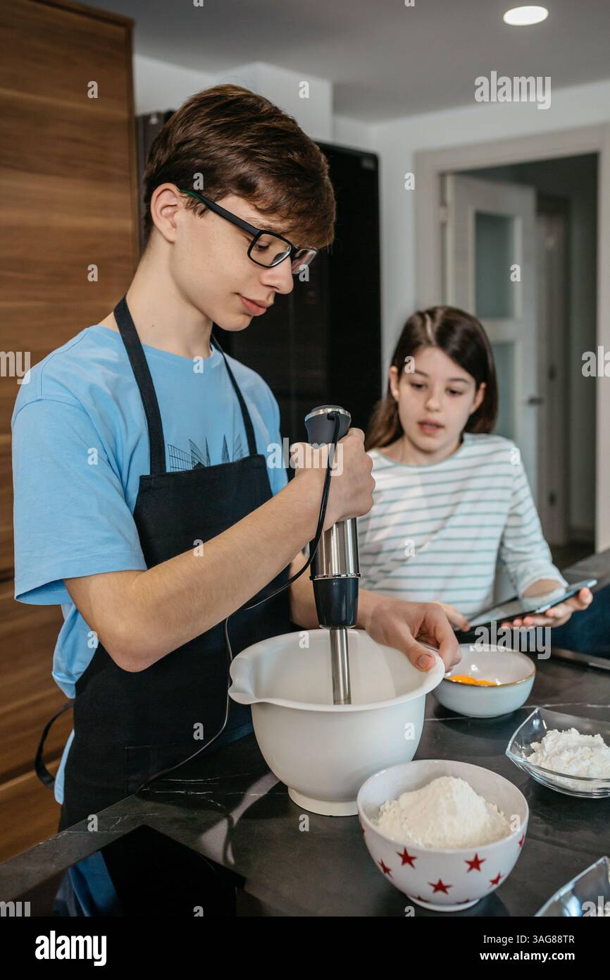 Brother and sister cooking together while following recipe on tablet ...