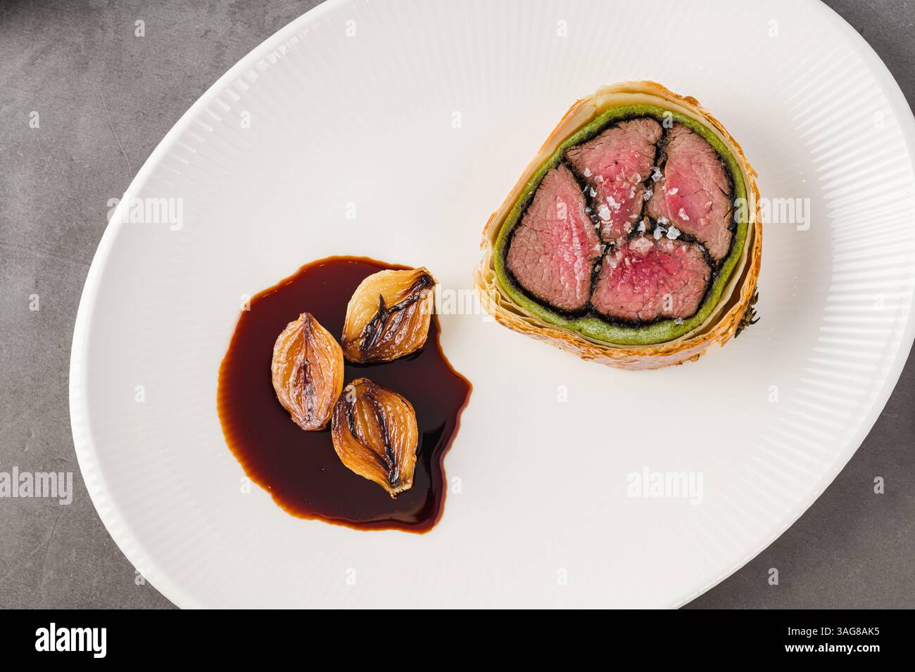 Modern plate of Beef Wellington, caramelized shallots and dark sauce ...