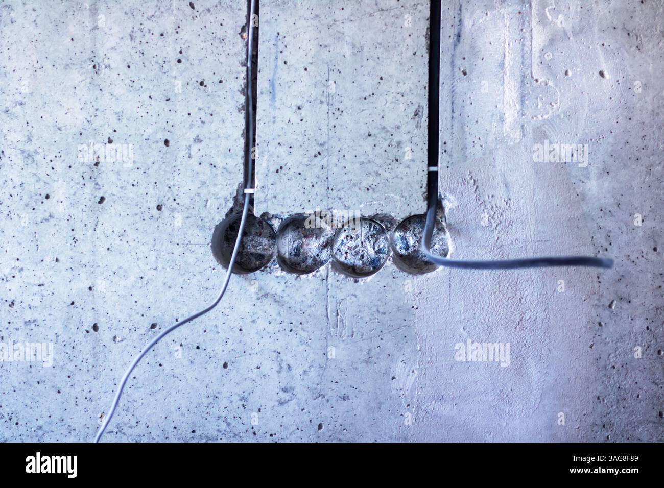 A bunch of various wires are hanging down from a rough concrete wall ...