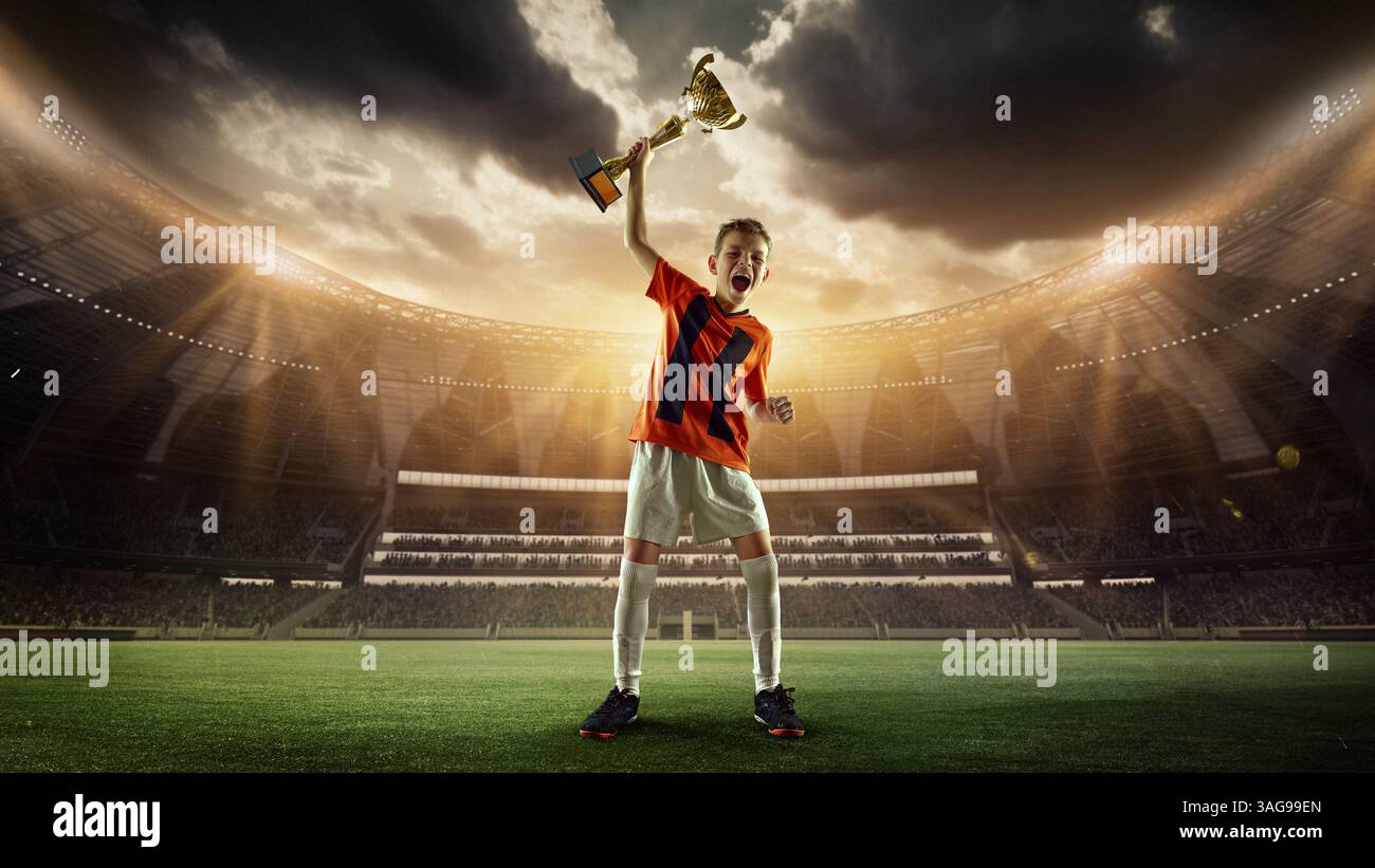 Happy and excited teen boy in orange jersey raising golden trophy with ...