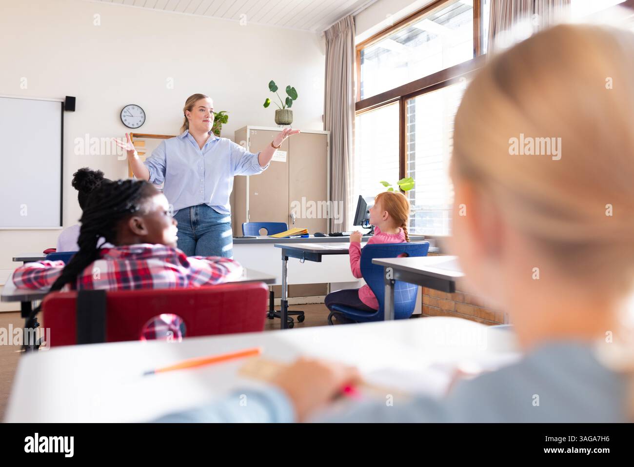 Female teacher explaining lesson to diverse students in classroom with ...