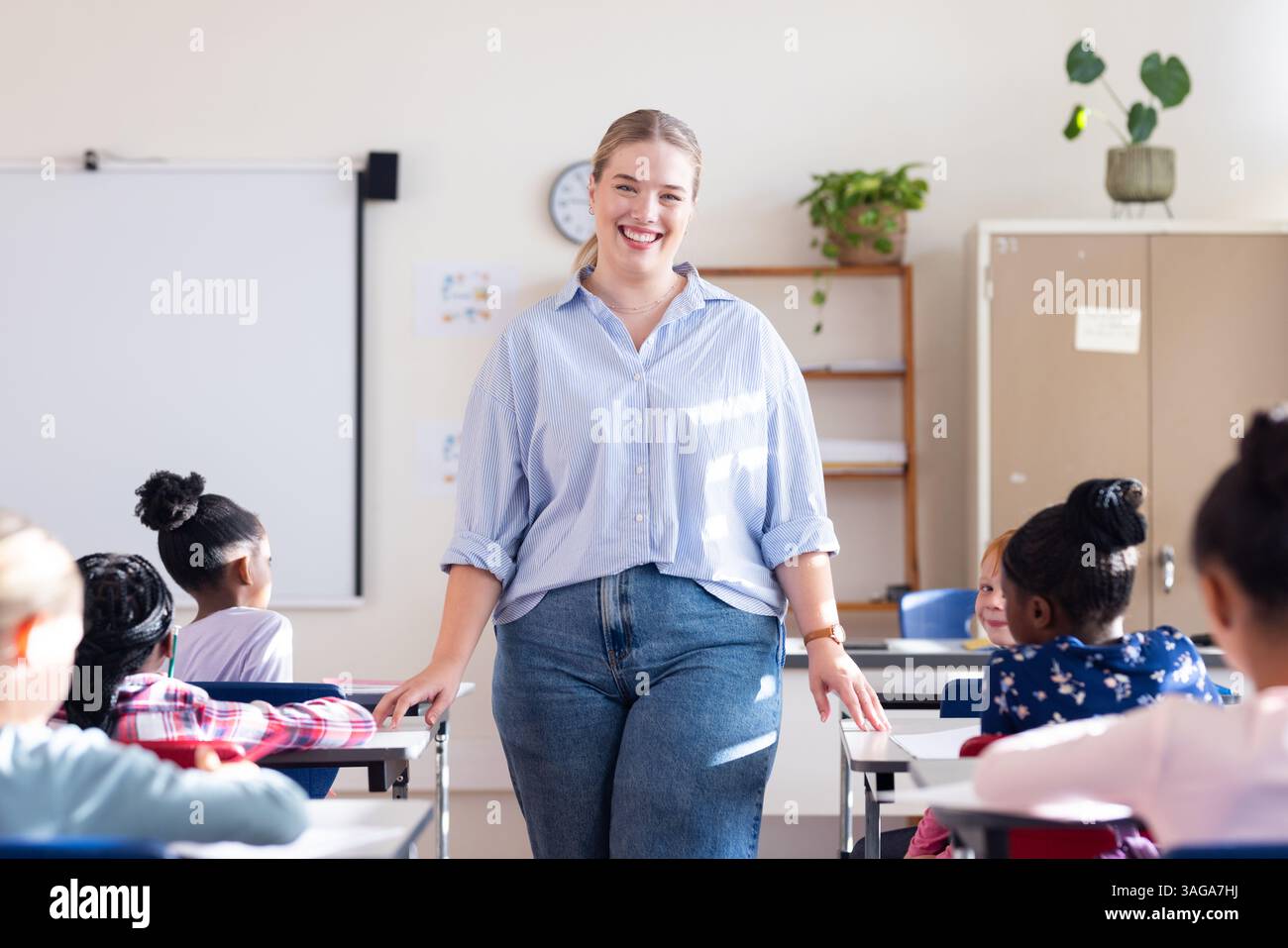Smiling female teacher standing in classroom with diverse students ...