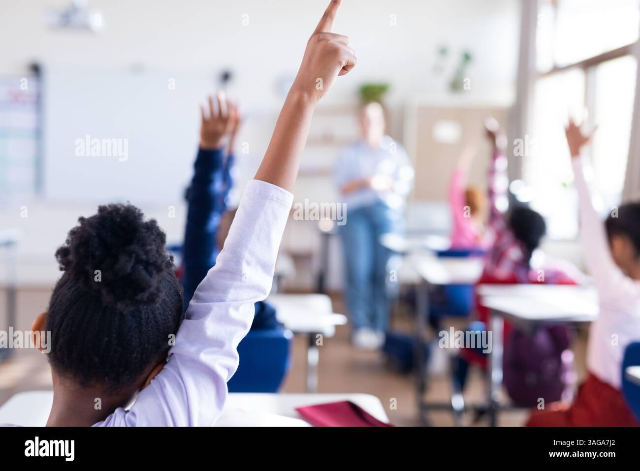 In school, diverse students raising hands in classroom, engaging with ...