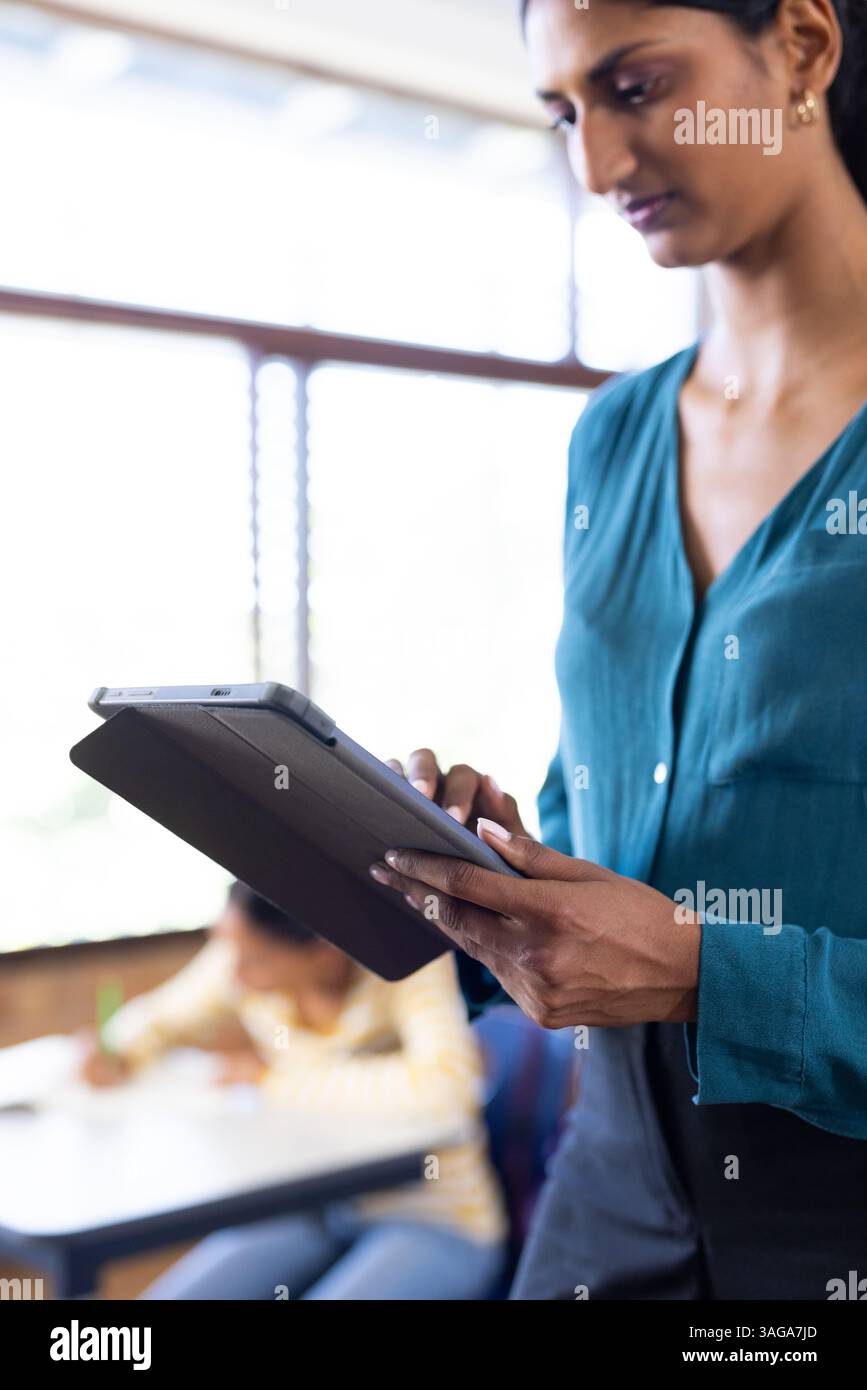 Using tablet, Indian female teacher managing classroom activities while ...