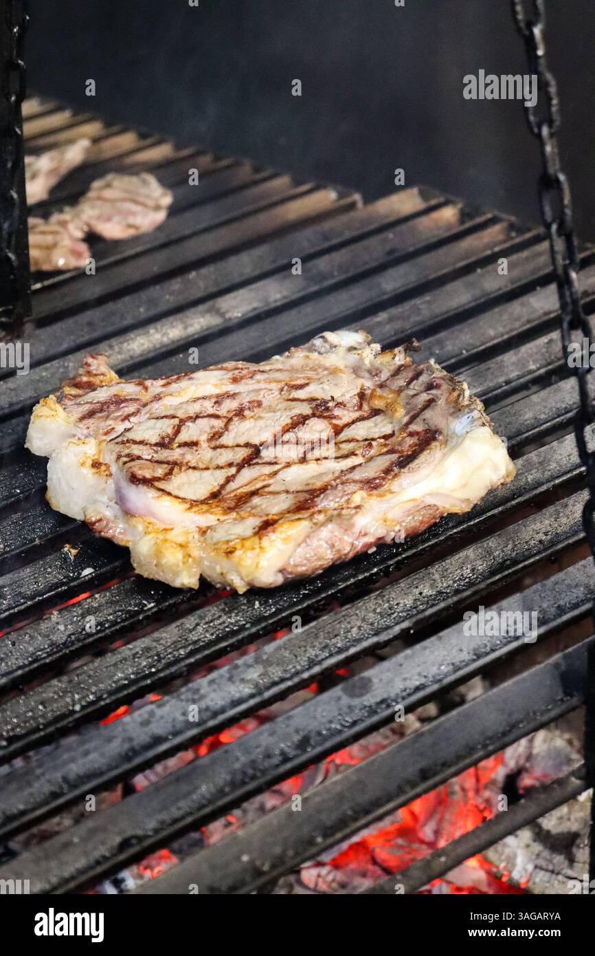 thick, juicy ribeye steak sizzling on a charcoal barbecue grill. The ...