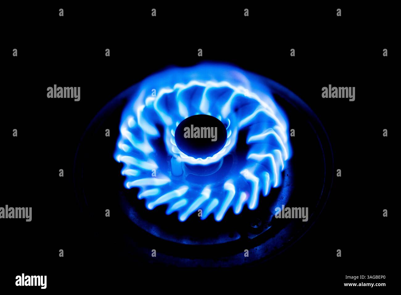 A gas stove burner with a bright blue flame, glowing against a dark ...