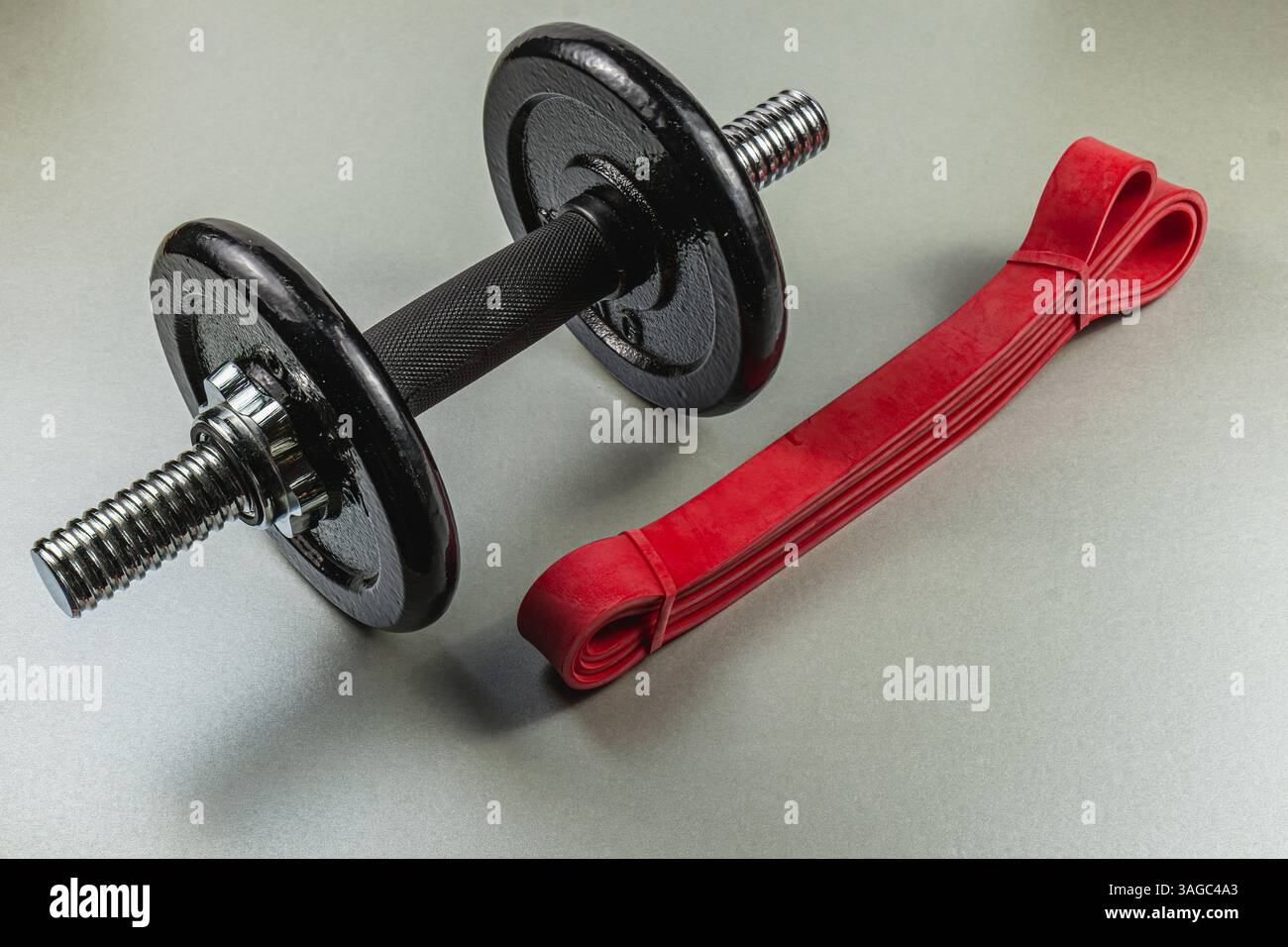 A black dumbbell rests on a smooth surface beside a red resistance band ...