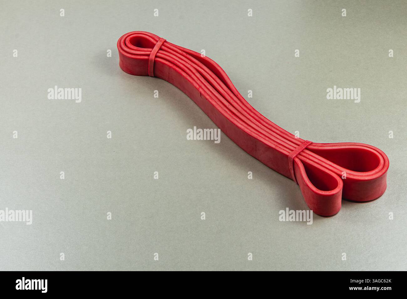 A red rubber band is placed flat on a gray surface, showcasing its ...