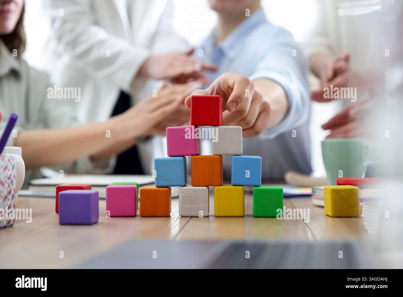 Unity concept. People building pyramid of colorful cubes at table ...