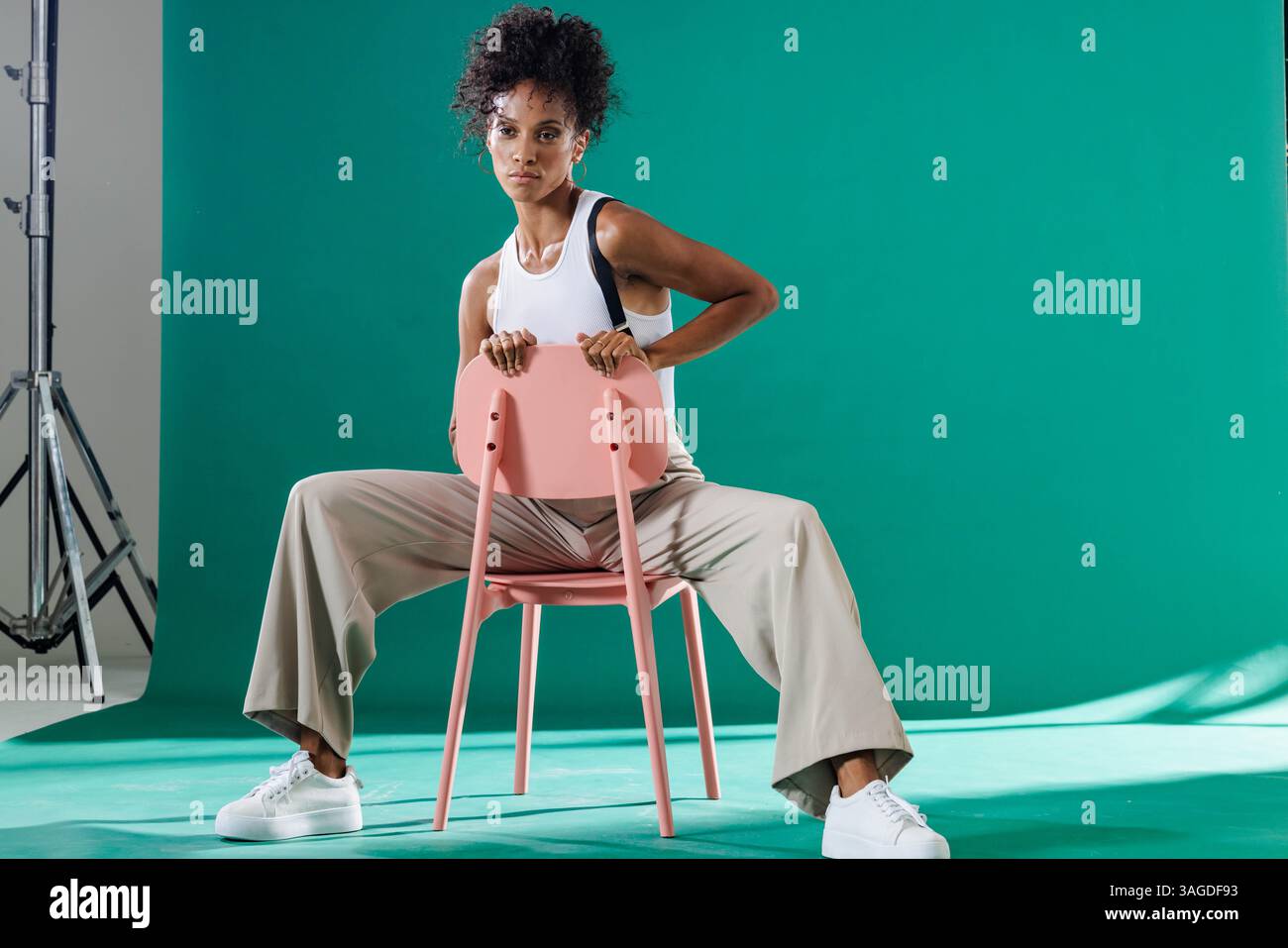 Confident woman sitting on chair in studio, embracing bold fashion ...