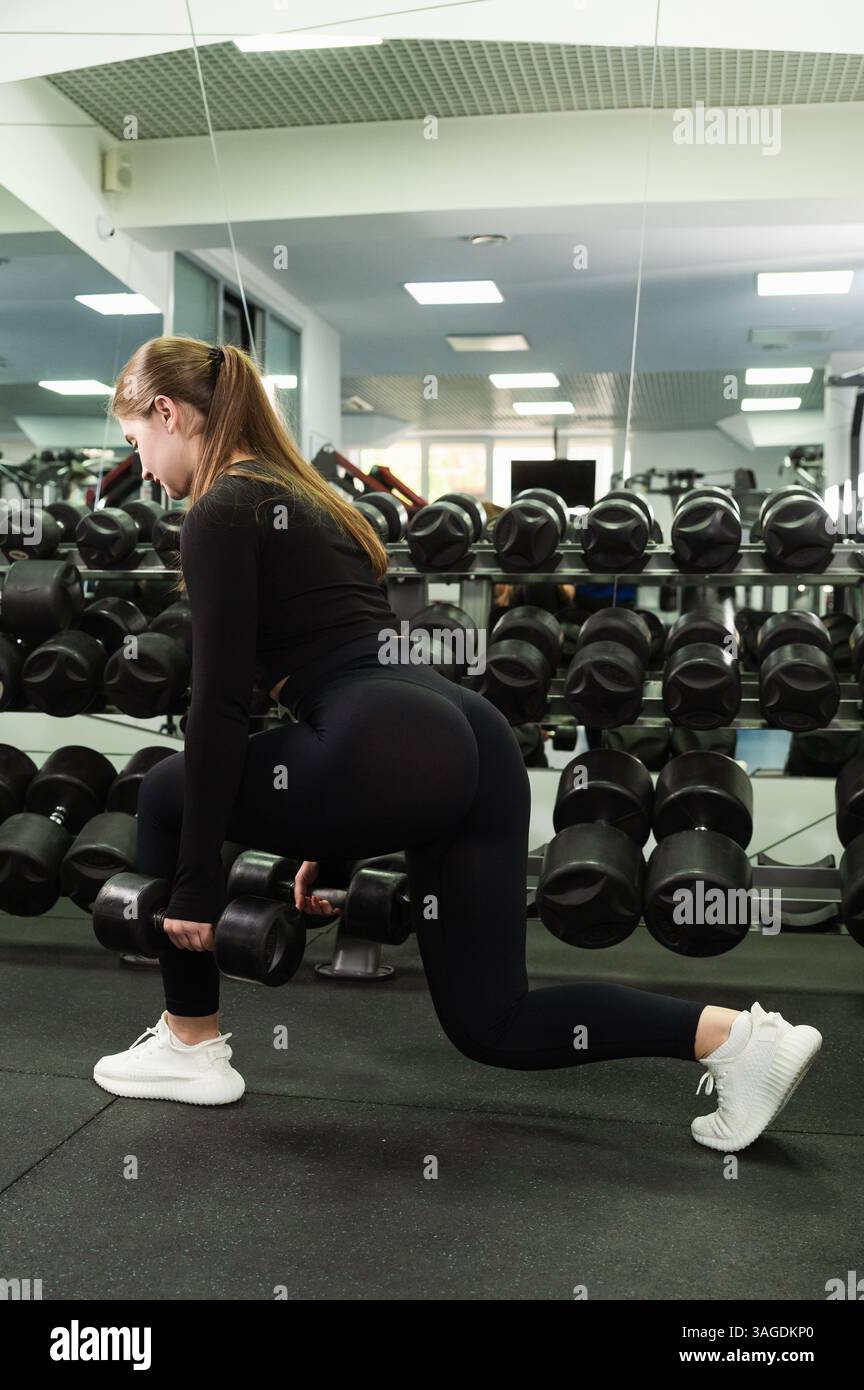 Fit young woman in black outfit performing dumbbell lunges in front of ...
