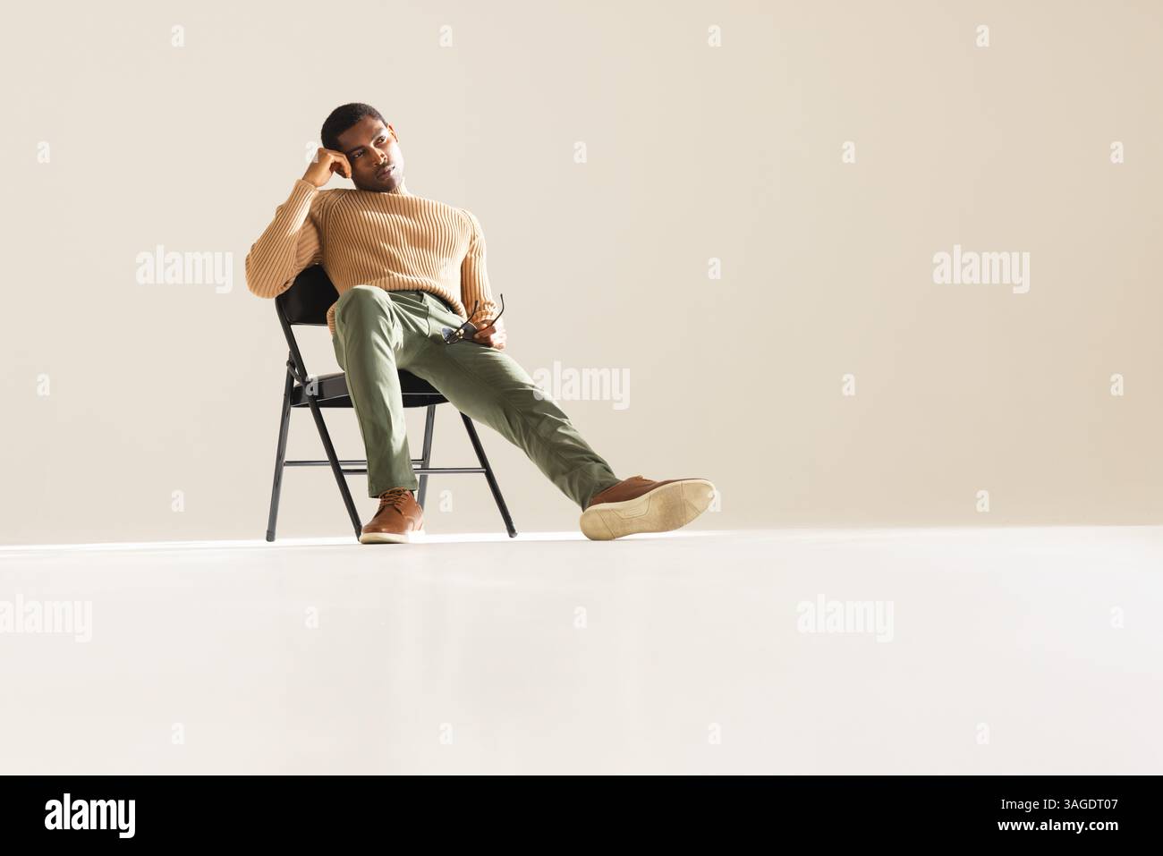 African American man in stylish outfit sitting on chair, looking ...