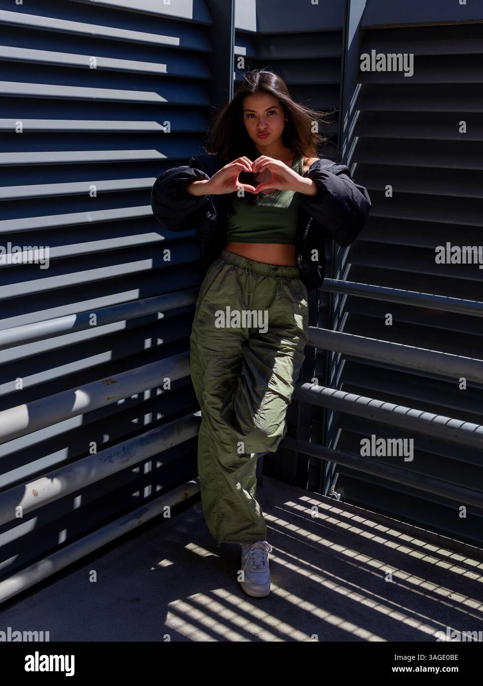 Gen Z woman looks at the camera and makes a heart sign with her hands ...