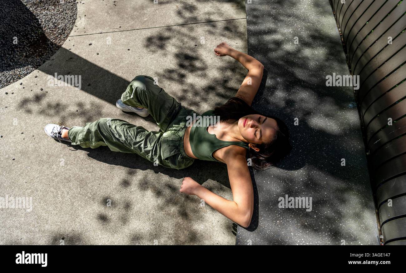 Gen Z woman lying down on the concrete in the park on a sunny day of ...