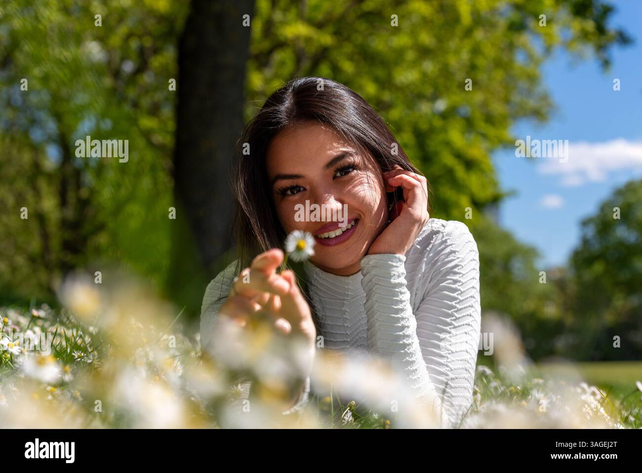 Portrait of a Gen Z woman lying in grass between flowers on a sunny day ...