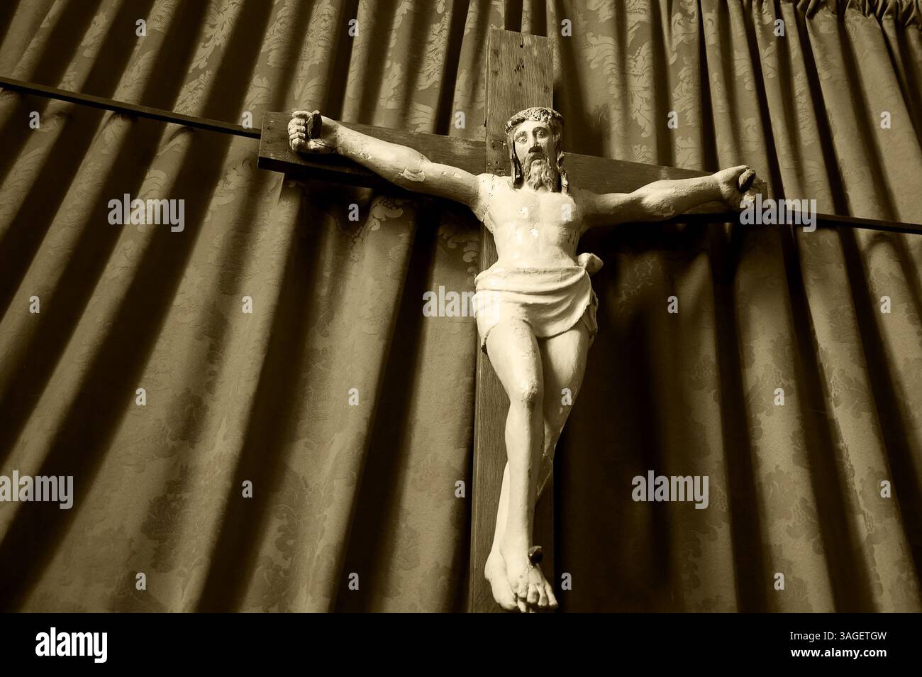 Old wooden crucifix of Jesus Christ isolated on drapery background in medieval church. Sepia ...