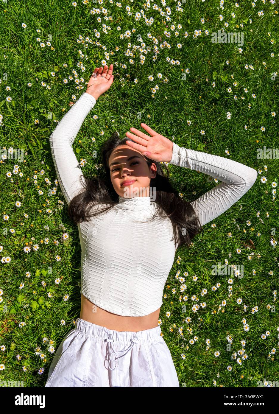 Portrait of a Gen Z woman lying in the green grass on a sunny day ...
