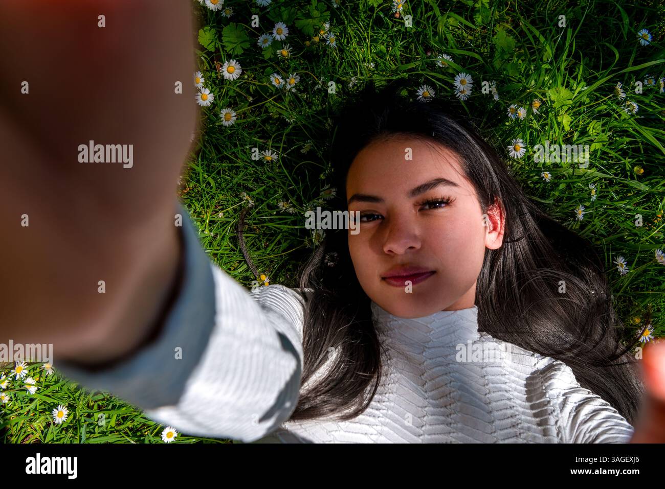 Gen Z woman taking a selfie picture while lying down on the green grass on a beautiful sunny day ...