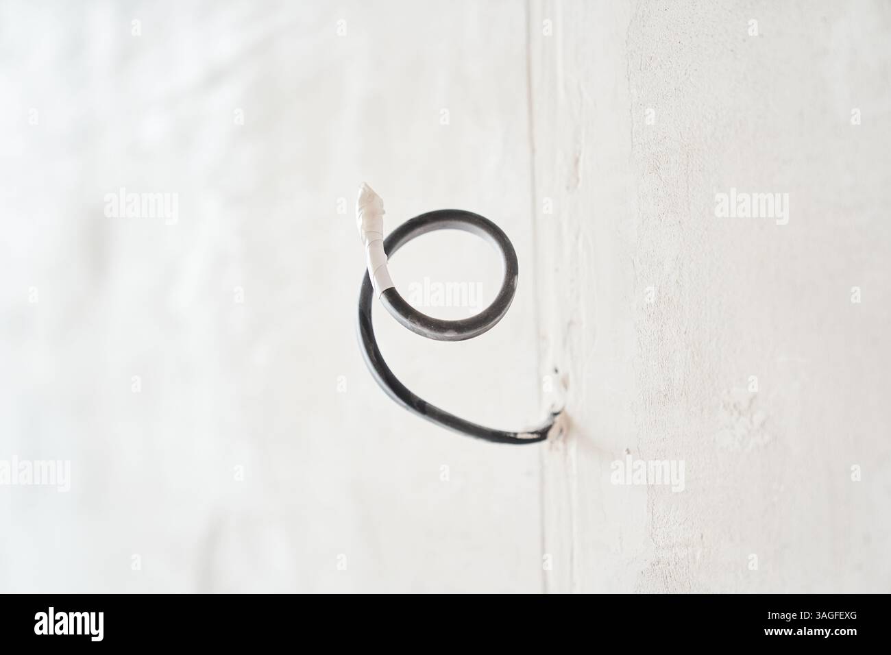 A black electrical wire protruding from a white wall. Electrical work ...
