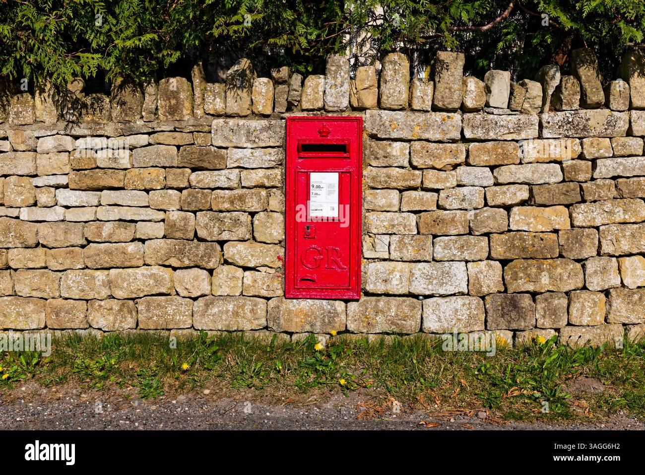A red letter box mounted in a dry stone wall in the Cotswold village of ...