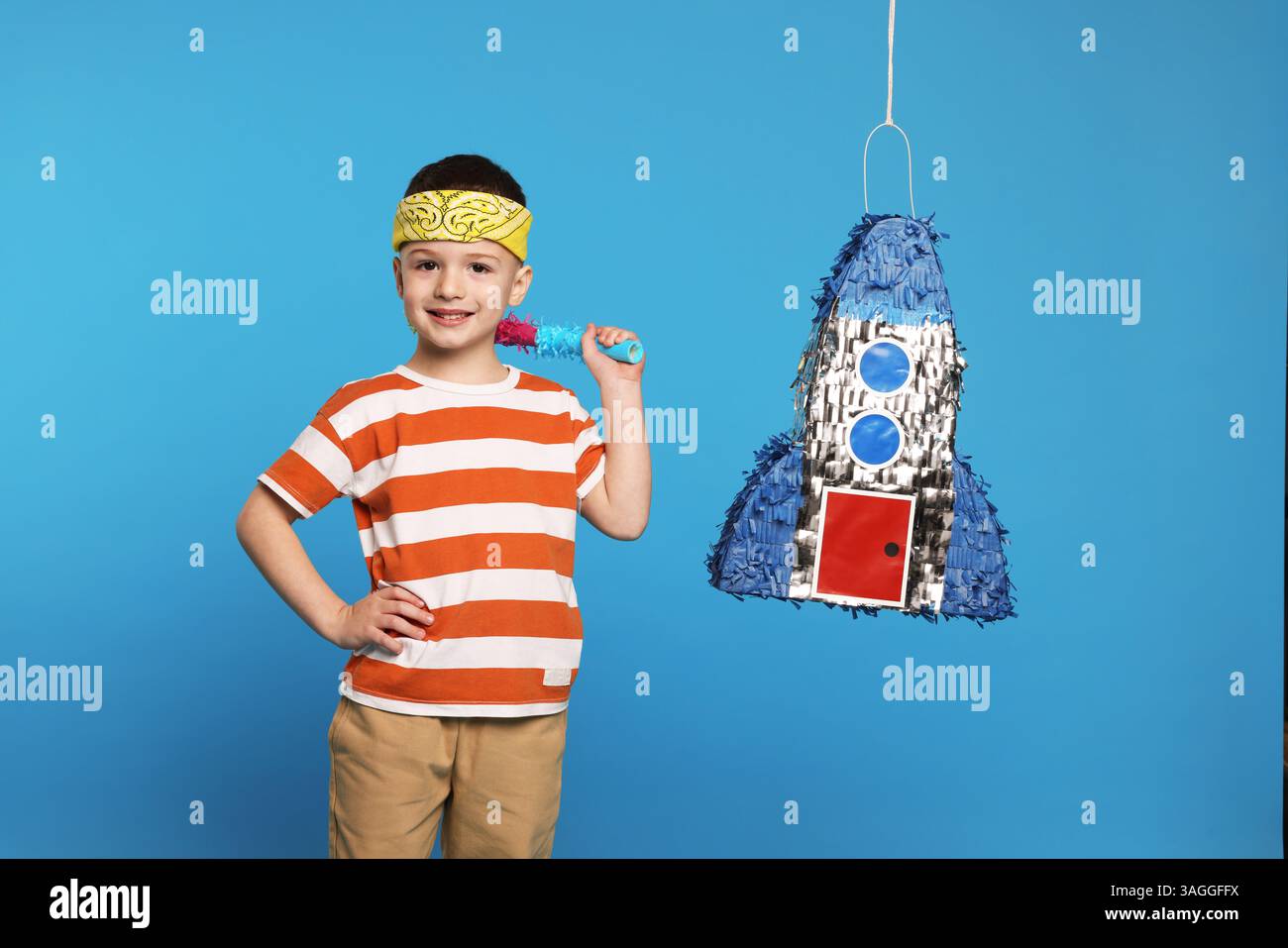 Happy boy with rocket shaped pinata and stick on light blue background ...