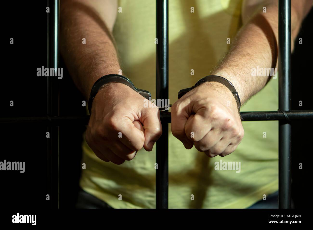 An arrestee with clenched fists and handcuffed behind bars Stock Photo ...