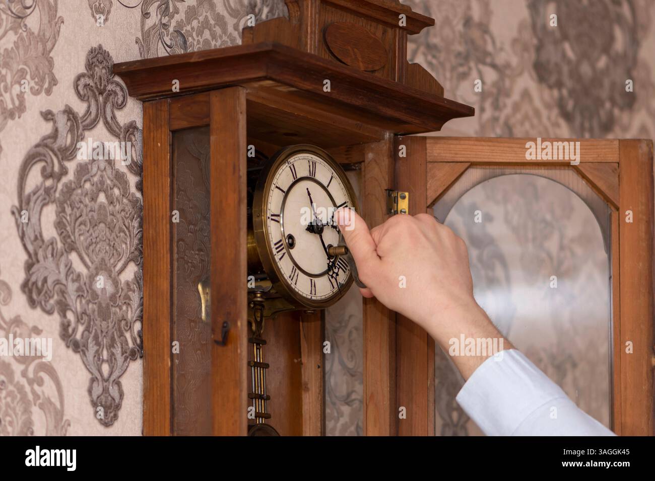 Time Transition: A man moves the hands on a classic pendulum clock ...