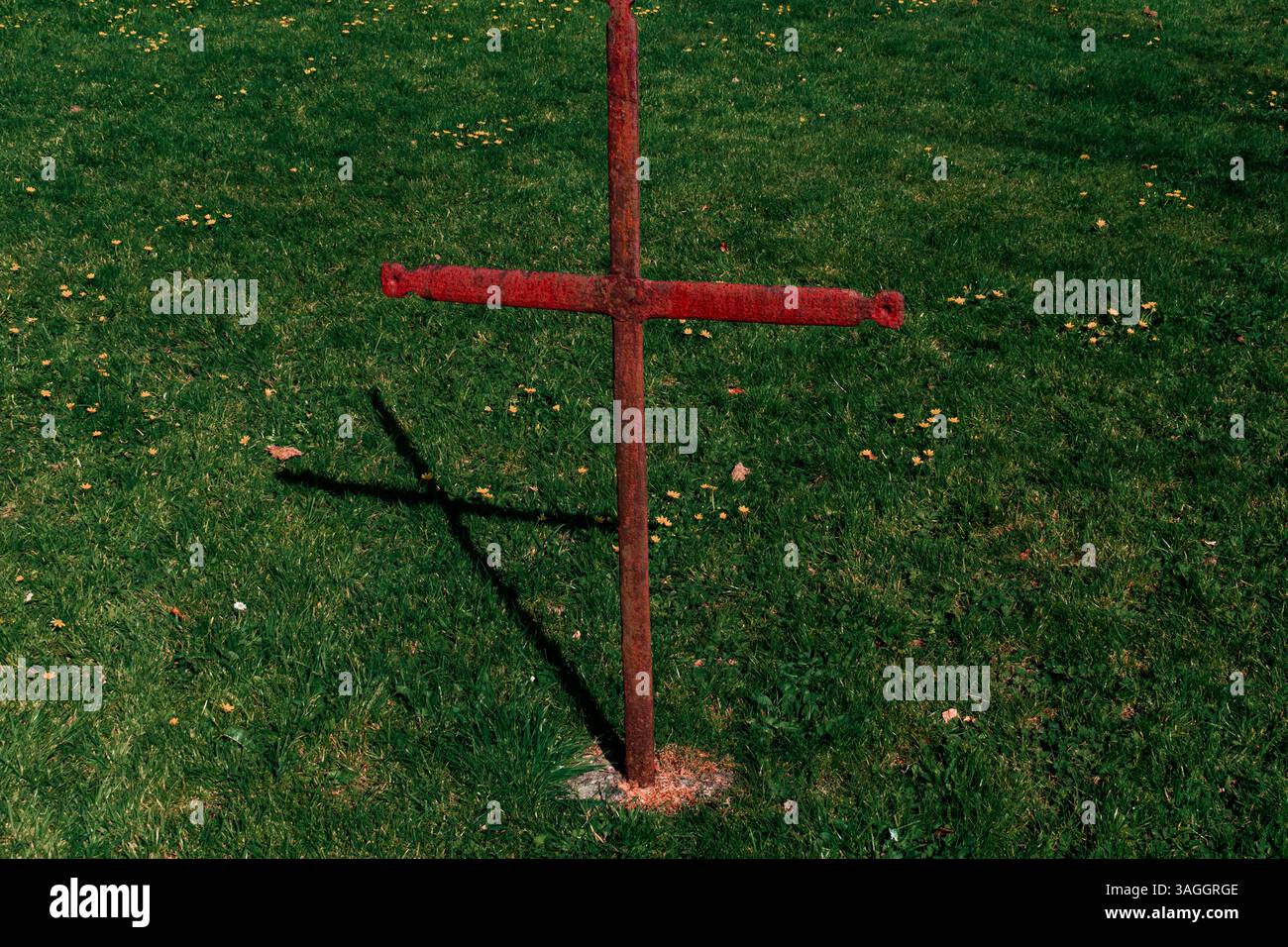 Red rusty cross with black shadow on grass background with copy space ...