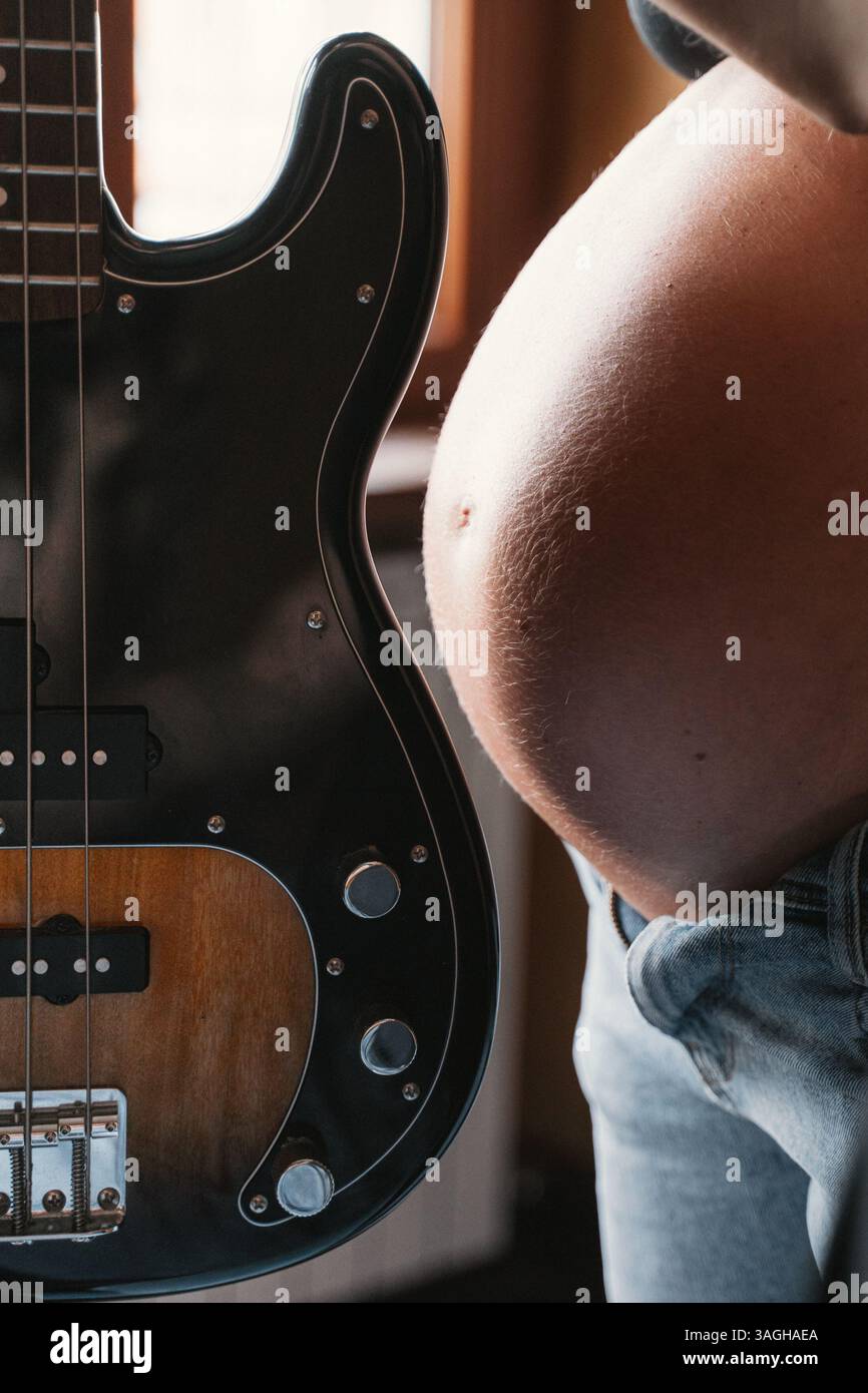Close-up image of a pregnant belly next to an electric bass guitar ...