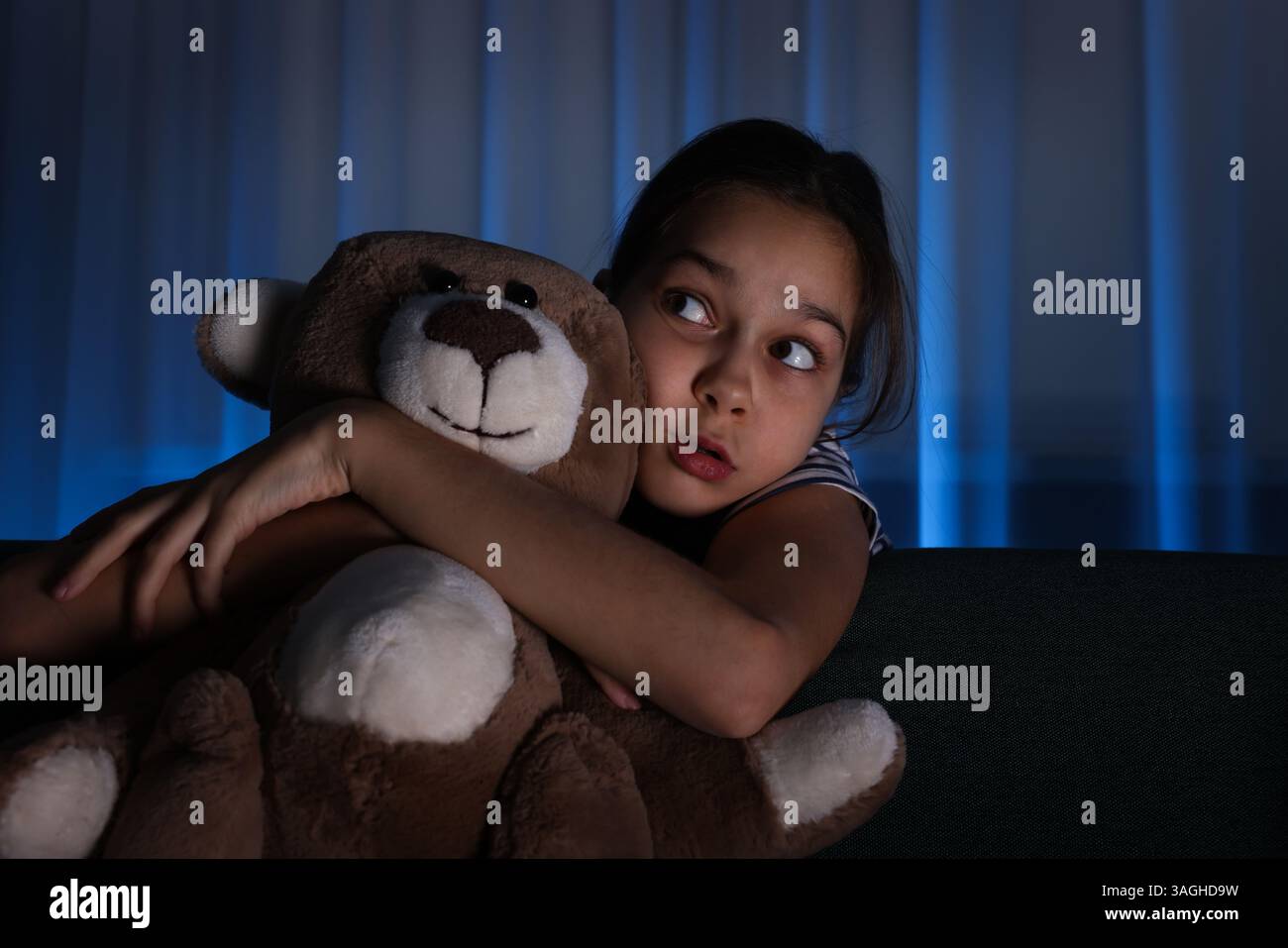 Scared girl with teddy bear hiding behind sofa at night Stock Photo - Alamy