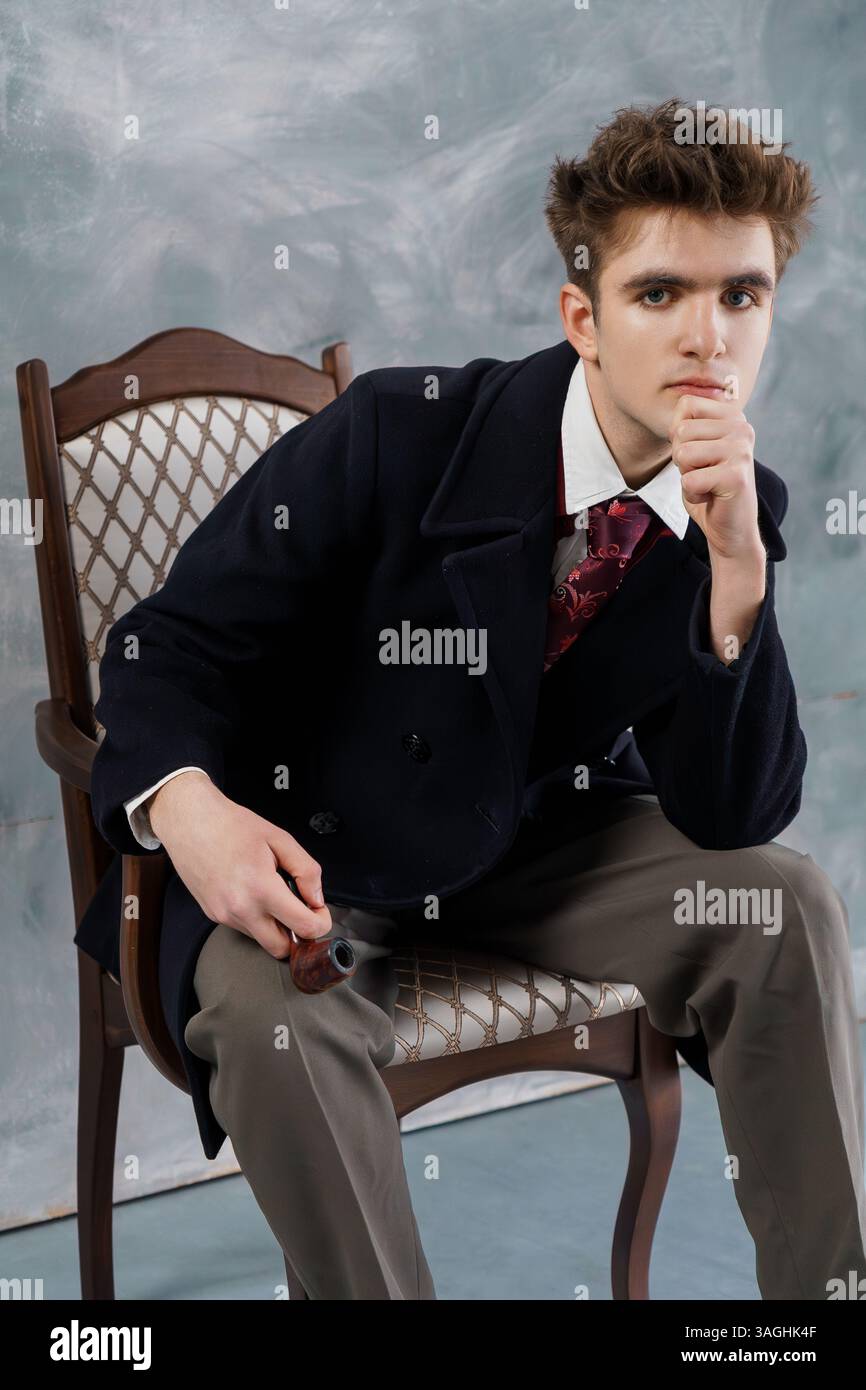 Young man in vintage attire sitting on ornate chair with a pipe ...
