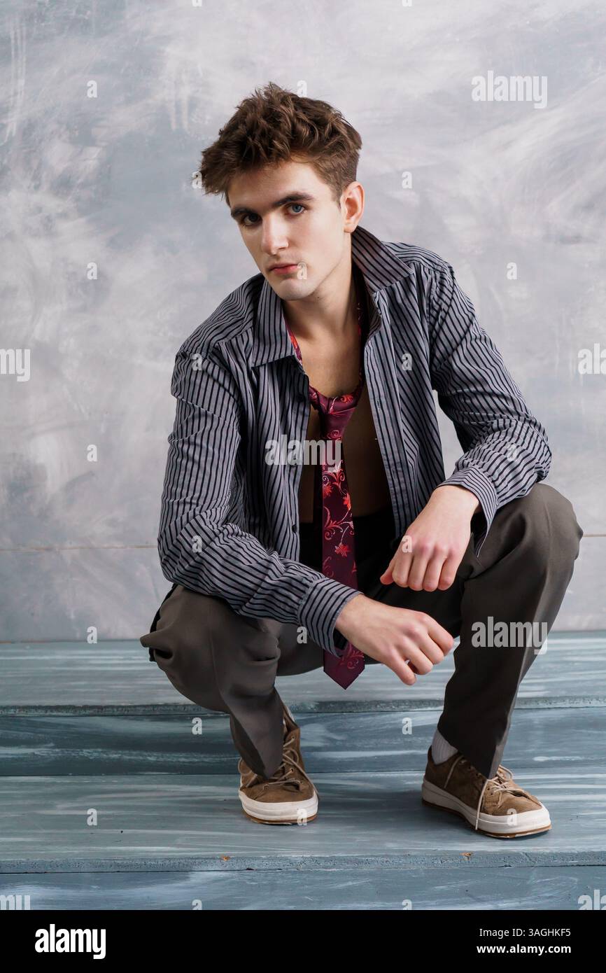 Young man in striped shirt and trousers crouching with tie loosely ...