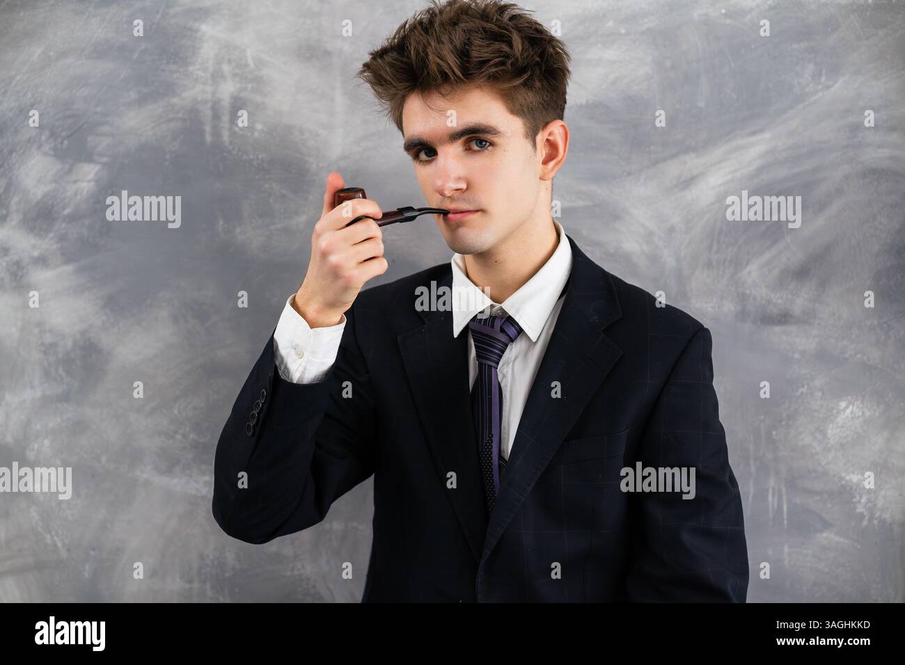 Young man in a suit thoughtfully smoking a pipe against a textured ...